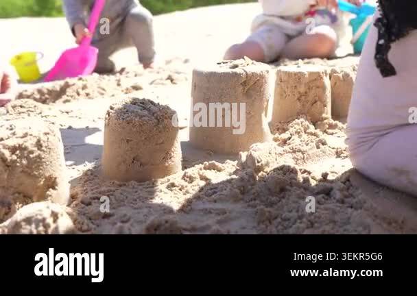 Children playing in sandbox building multiple sandcastles with plastic ...