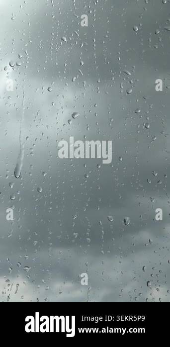 Rain drops on glass window with the background of grey moody sky close ...