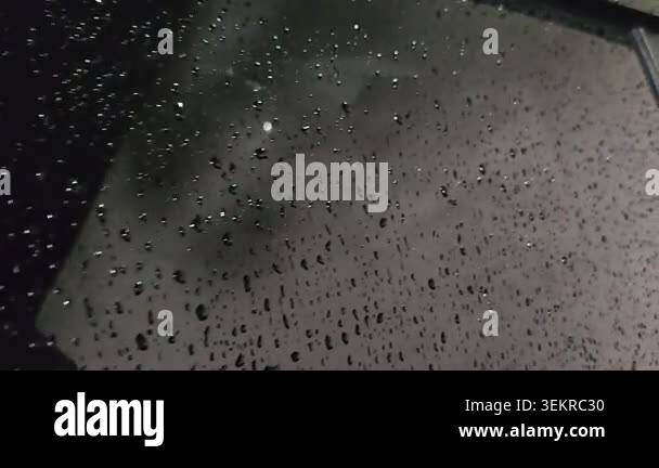 Close-up view of raindrops covering a car window during nighttime, with ...