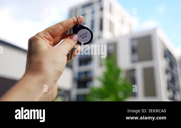 Hand holding house keys with My First Home keychain near modern ...