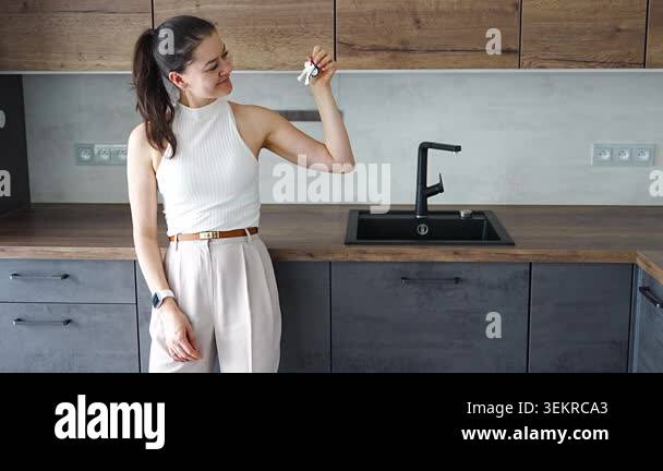 Young woman standing in modern apartment kitchen and holding house keys ...