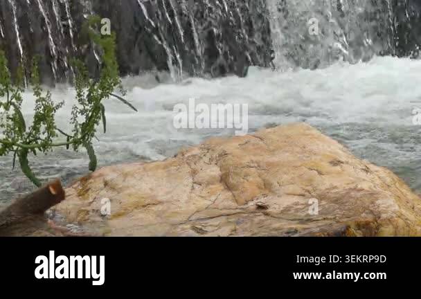 Large natural rock in the foreground with a fast rushing river ...