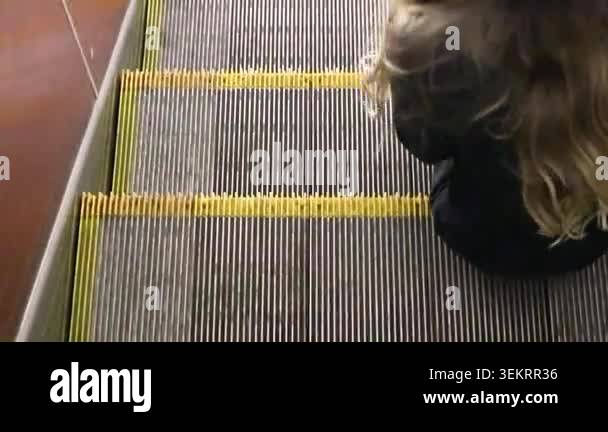 A teenage girl sits on the moving steps of a subway escalator with ...