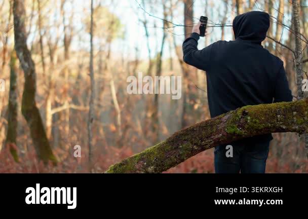 Slow motion. Man in black hoodie standing behind mossy branch in forest ...