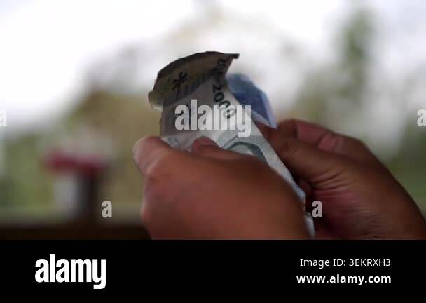 Close-up of a person's hands counting crumpled two thousand Indonesian ...