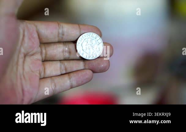 Close-up detail of an antique Indonesian 25 Sen coin on fingertips, a ...