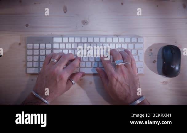 Close-up of hands typing on a modern white keyboard at a wooden desk ...