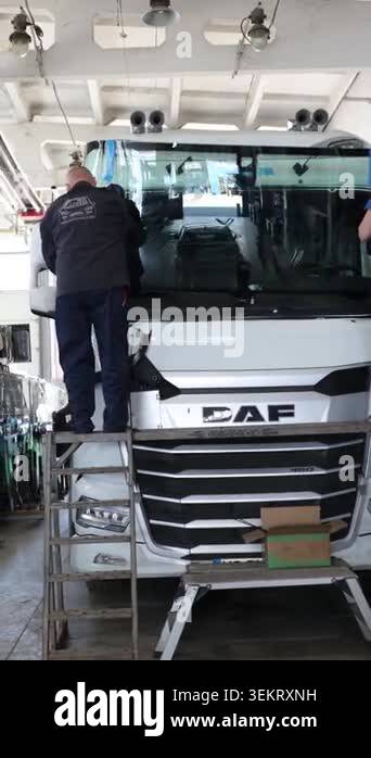 Workers install windshields on a large truck in a repair shop. Men ...