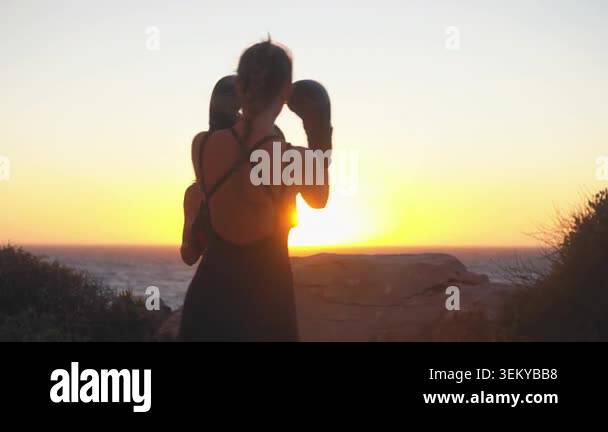 Sporty female fighter practicing boxing on hill overlooking seascape ...