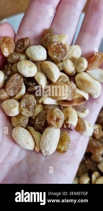 A close-up view of a person hand holding a mixture of roasted peanuts ...