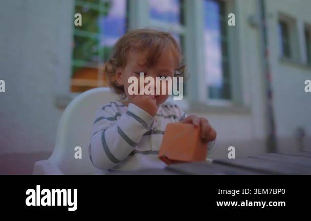 Young child playing with cube shaped container at family cafe table ...