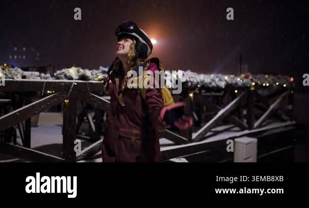 Happy snowboarder girl dances in the falling snow at night at a ski ...
