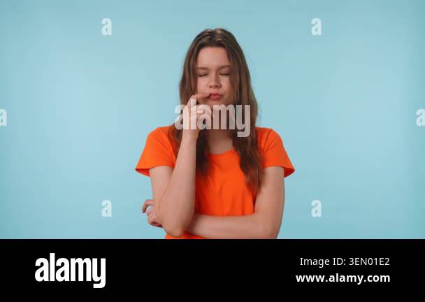 A woman wearing an orange shirt ponders thoughtfully against a blue ...