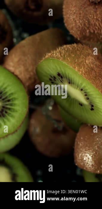 Sliced pieces of kiwi fly on a black background. Filmed on a high-speed ...
