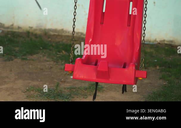 Front view of a red plastic swing for children suspended by chains in ...