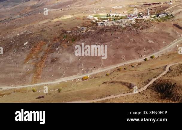 Wide aerial view of a remote hillside settlement with dirt roads, small ...