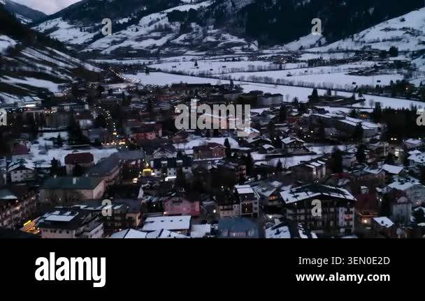 Wide aerial view of a snow-covered alpine town at dusk, surrounded by ...