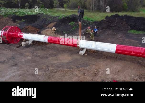 Large red and white pipeline section lies across a muddy construction ...