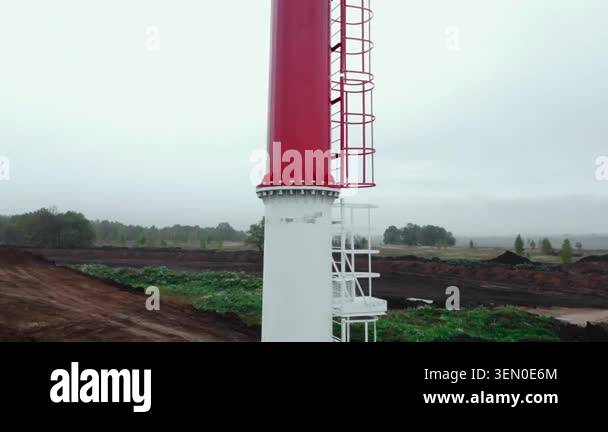 A tall red and white industrial tower rises above a muddy construction ...