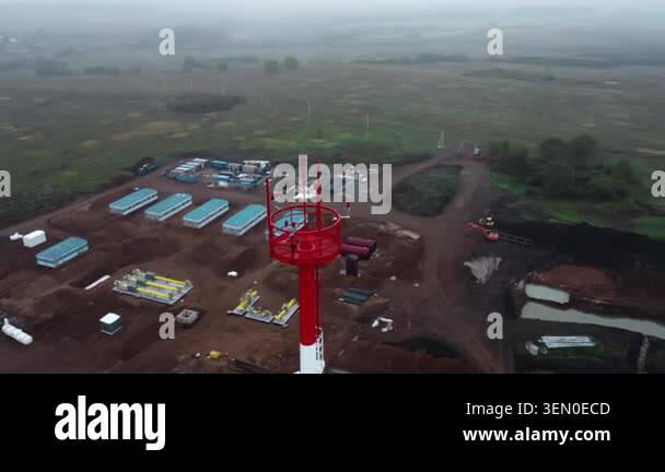 High aerial view of a large industrial worksite showing a tall red and ...