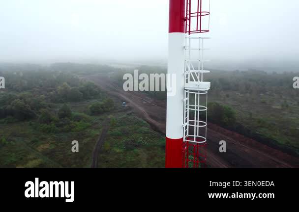 A tall red and white communication tower stands beside a dirt road over ...
