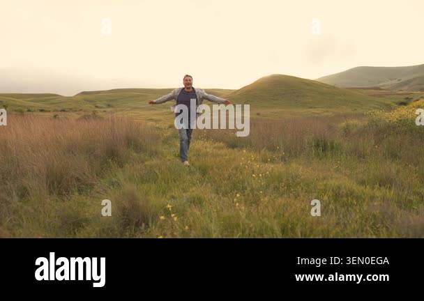 A joyful person sprinting through a grassy meadow with mountain ...