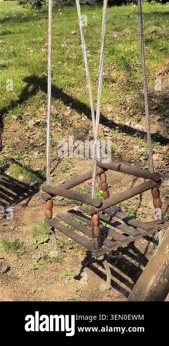 Real time vertical video of an old rustic wooden swing with worn brown ...
