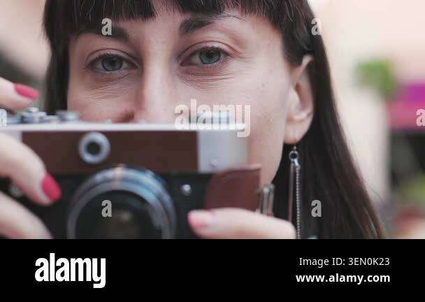 Close-up of a dark-haired woman holding a vintage camera near her face ...