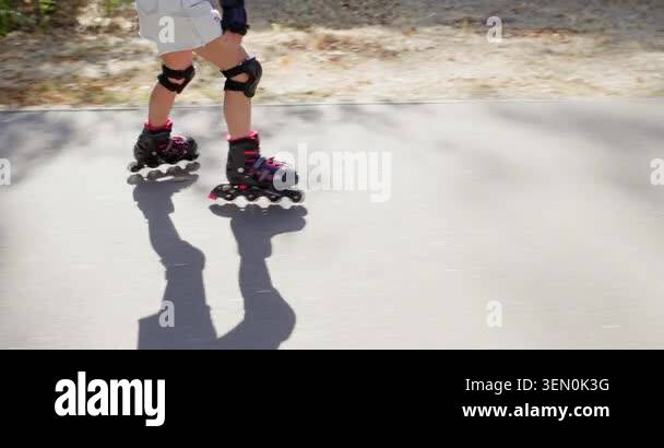 Girl skates along park pavement wearing protective knee pads. Child in ...