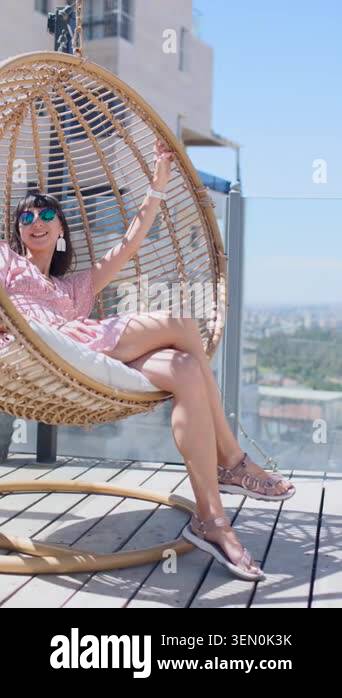 vertical video. A woman wearing sunglasses and a light pink dress sits ...