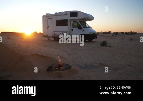 Off-grid camper van at sunset in the desert with a glowing campfire ...