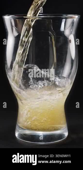 Refreshing pour of golden beer into a glass on black background close ...