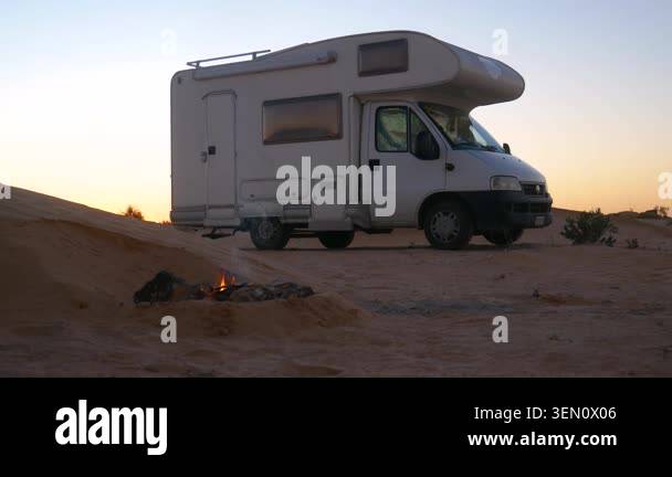 Off-grid camper van at sunset in the desert with a glowing campfire ...