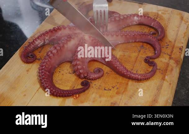 Chef is cutting a freshly boiled red octopus with a sharp knife on a ...