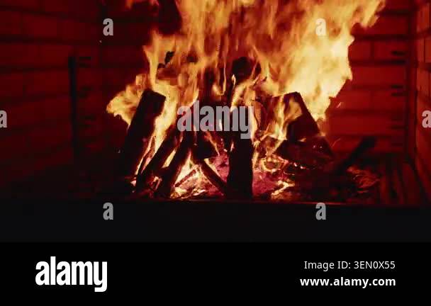 A cozy burning bonfire with bright orange flames and glowing logs ...