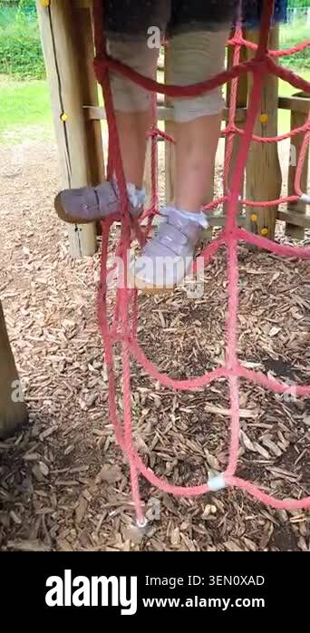 Close-up of the legs of a child climbing up a red rope climbing net on ...