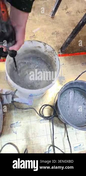A builder uses an electric drill-mixer to mix gray cement mortar for ...
