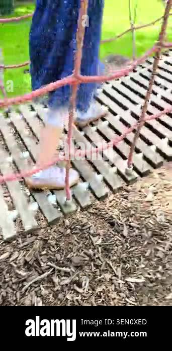 A little girl in a blue dress carefully walks across a swaying wooden ...