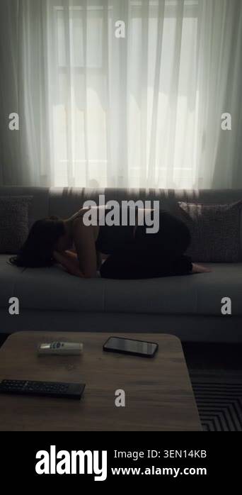 Young woman sitting curled up on sofa in emotional distress at home ...