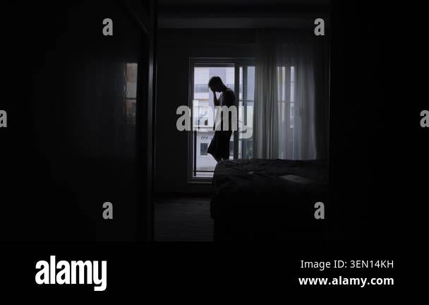 Silhouette of depressed man standing by bedroom window experiencing ...