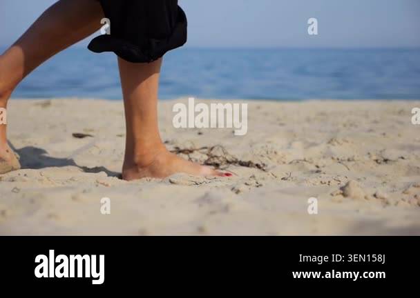 Female feet walking on sand at the beach with seascape at background ...