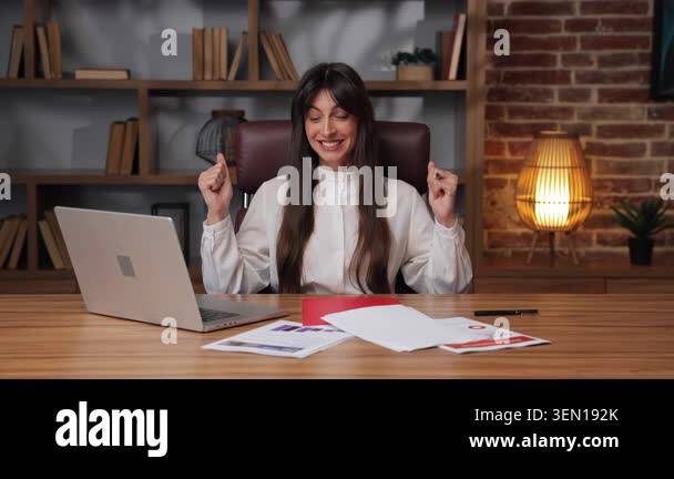 Business woman expresses happiness and delight at her desk. She raises ...