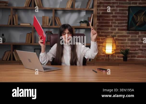 A happy business woman dances and holds documents at her desk. She ...