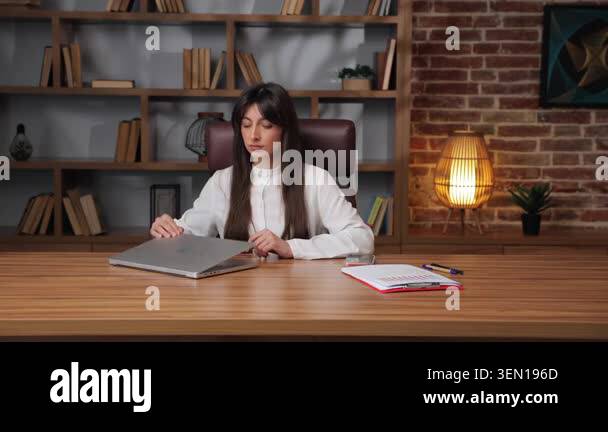 A Caucasian business woman walks into an office, sits down, opens her ...