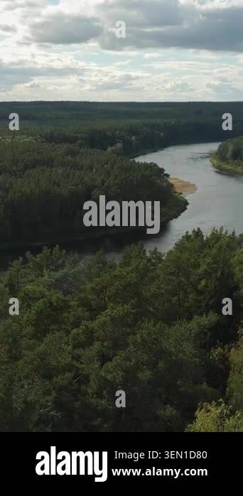 A serene river winding through a dense forest under a partly cloudy sky ...