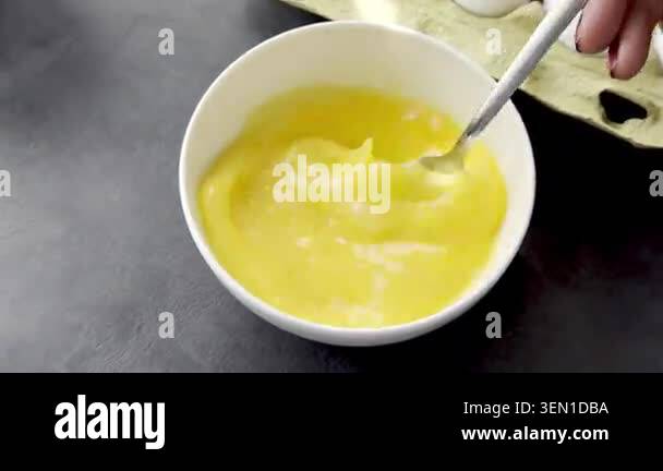 Close-up view of a hand mixing beaten eggs in a white bowl ...