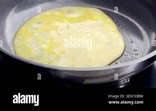 Yellow omelette cooking in a frying pan, gradually solidifying and ...
