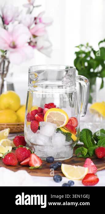 Adding blueberries to a large glass pitcher filled with ingredients for ...