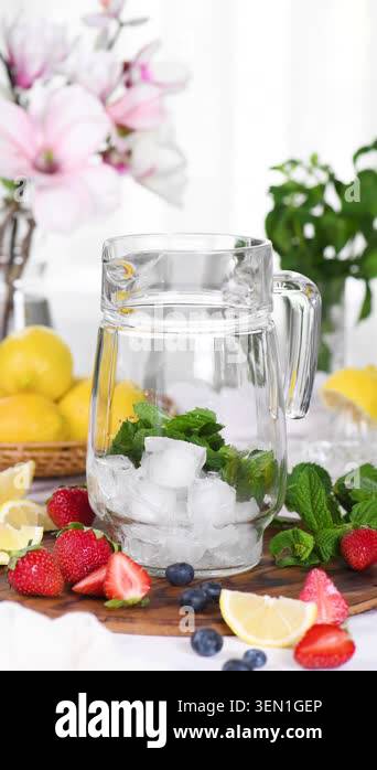 A woman's hand places thinly sliced lemon slices into a glass pitcher ...