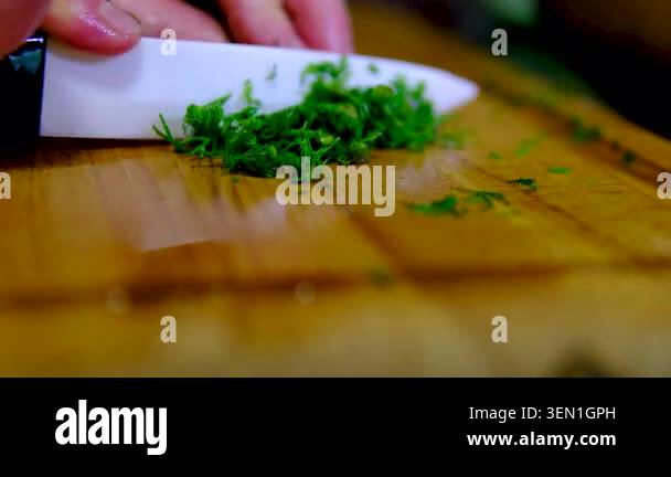 Fresh green dill is carefully sliced with a white ceramic knife on a ...